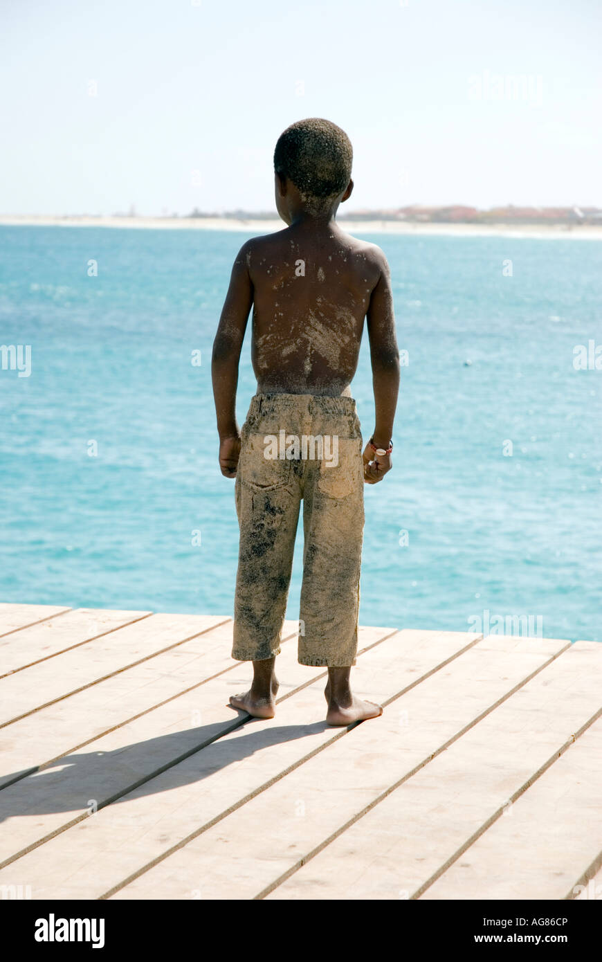 A young coloured boy standing on pier Stock Photo - Alamy