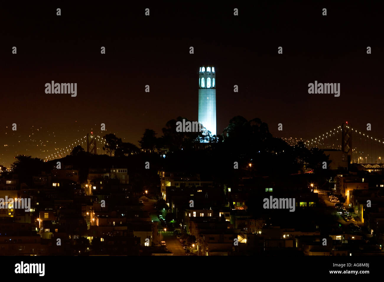 Coit Tower lit at night with the Bay bridge in the background and the ...