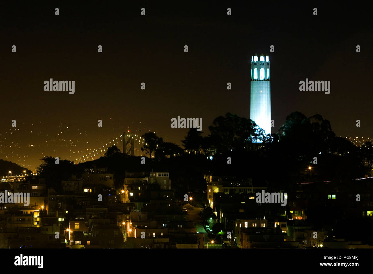 Coit Tower lit at night with the Bay bridge in the background and the ...