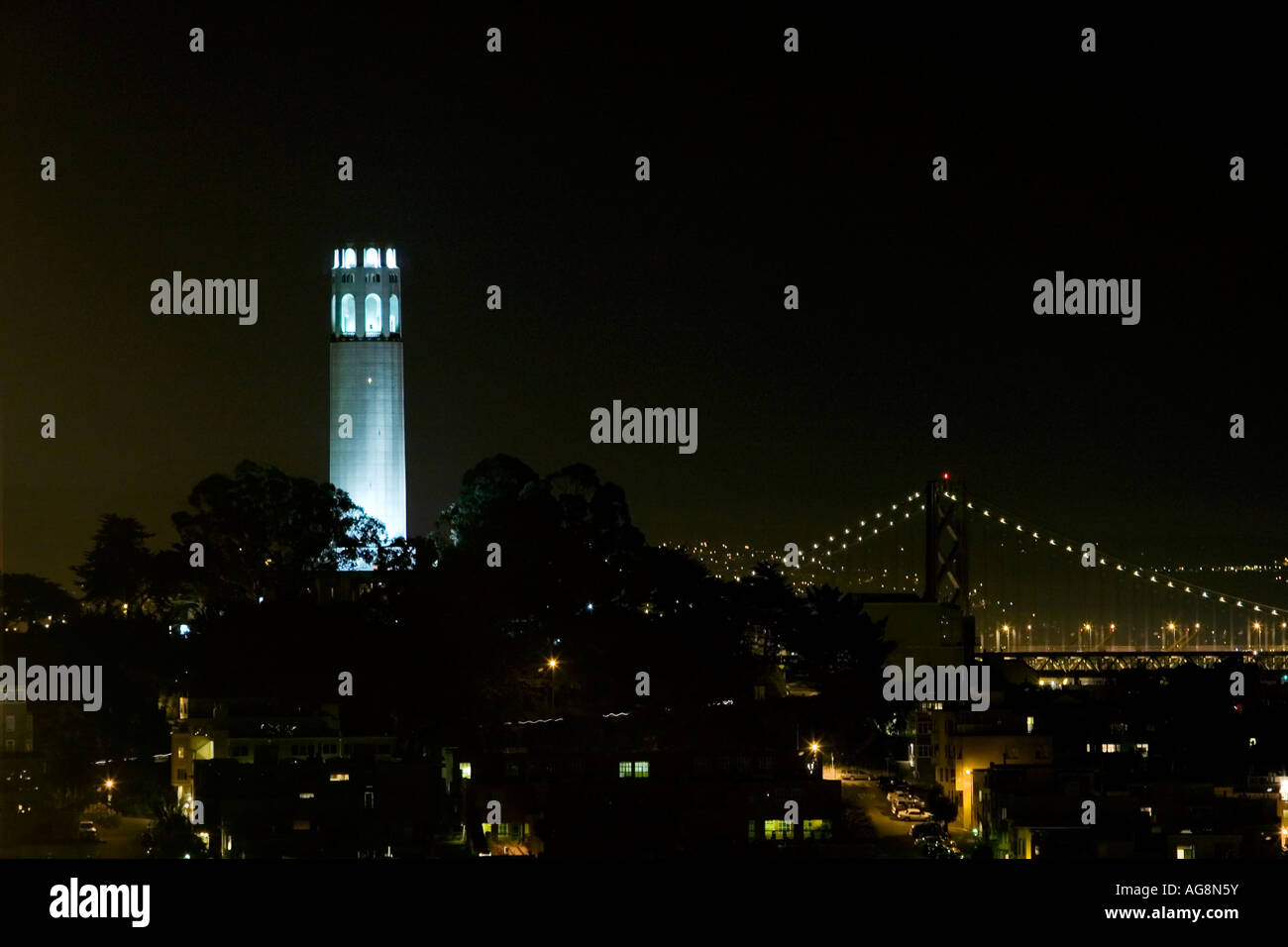 Coit Tower lit at night with the Bay bridge in the background and the ...