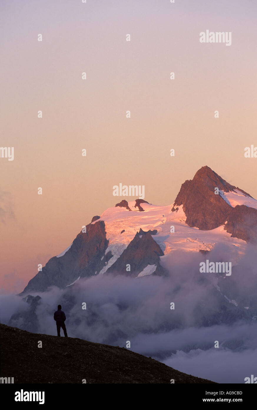 Hiker standing on ridge below Mt Shuksan at sunset North Cascades ...