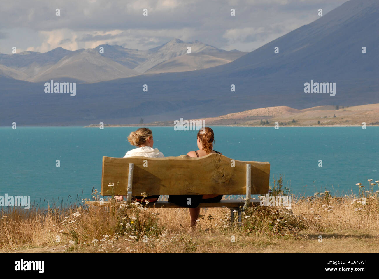 Rear view of two women sitting on a wooden bench and looking over at a ...