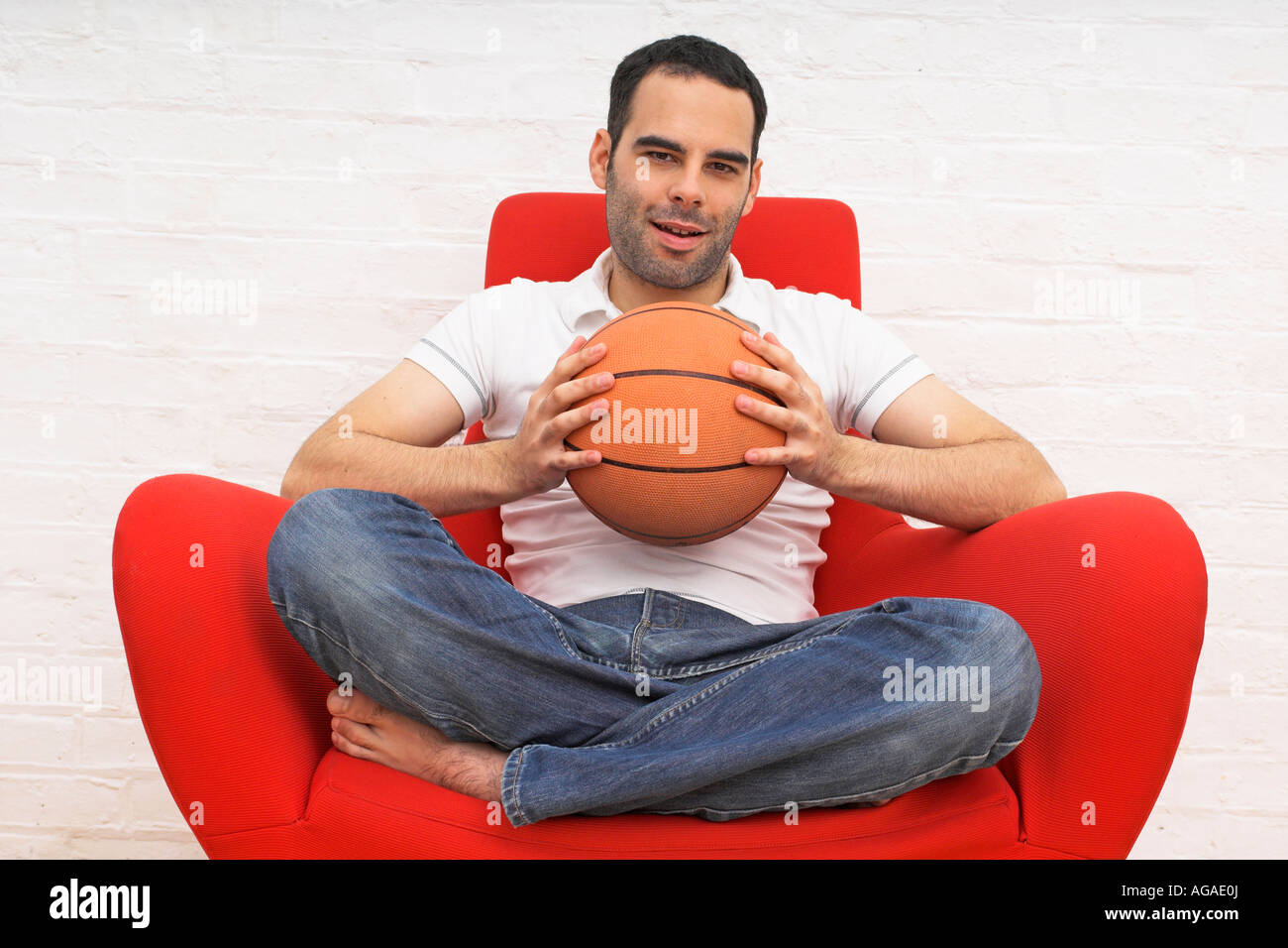 young man sitting on red arm chair holding basketball Stock Photo - Alamy