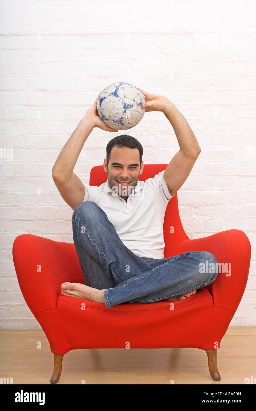 joyous young man sitting in red arm chair holding football Stock Photo ...