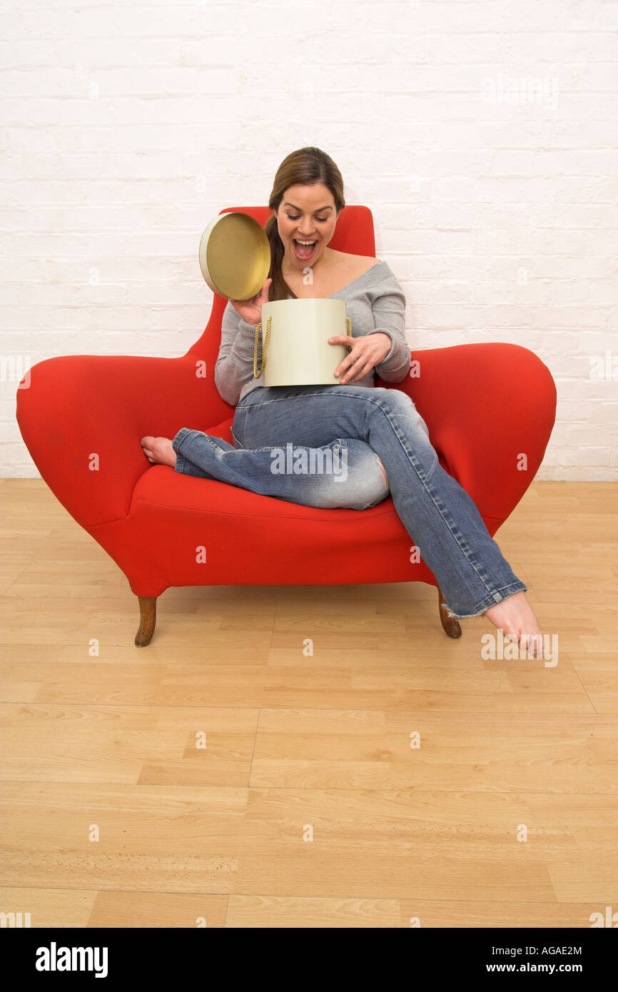 young woman sitting in red arm chair opening present Stock Photo - Alamy