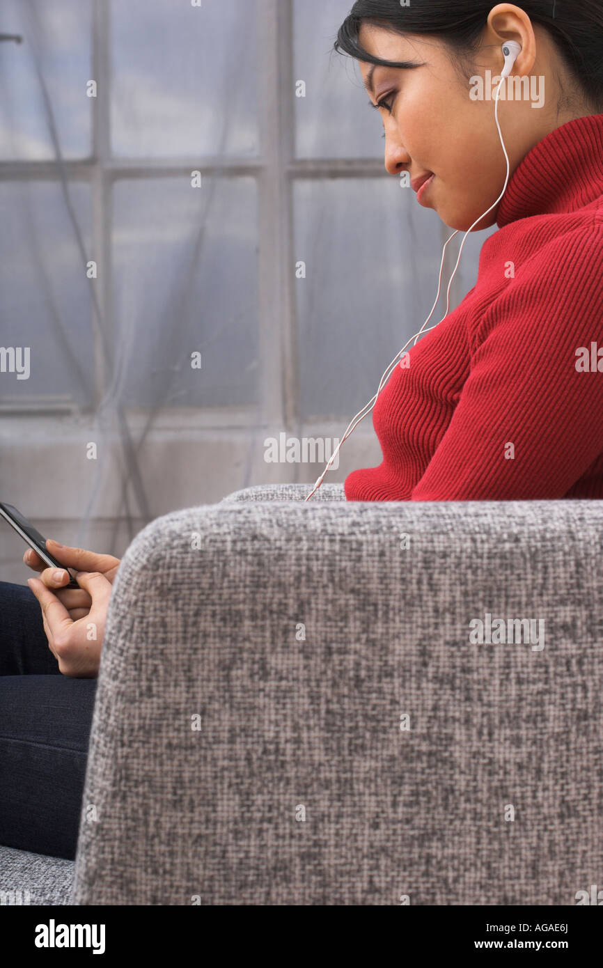side view of young japanese woman sitting in arm chair listening to ...