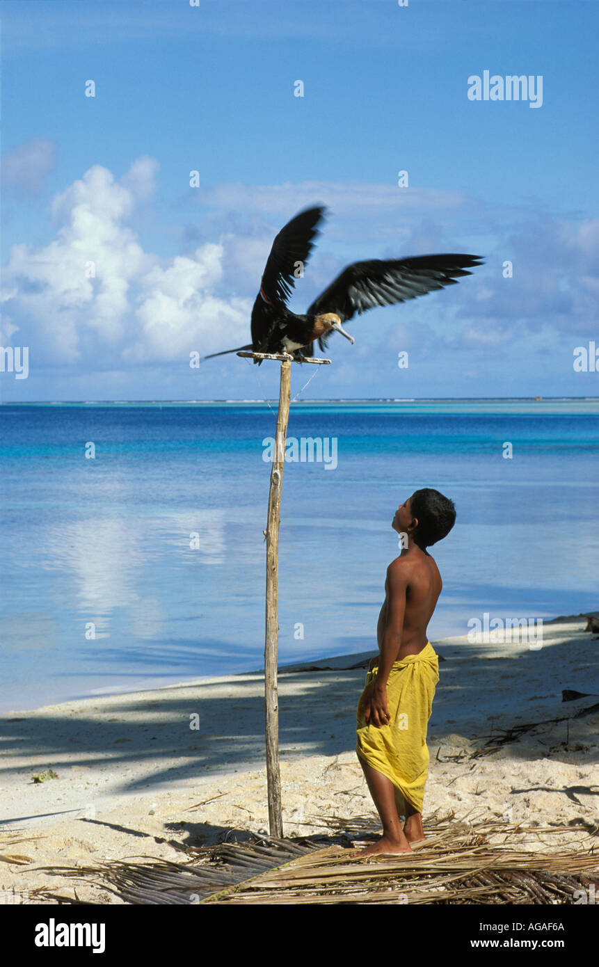 Boy and tame lesser frigate bird on a beach Ifaluk Atoll Yap State ...
