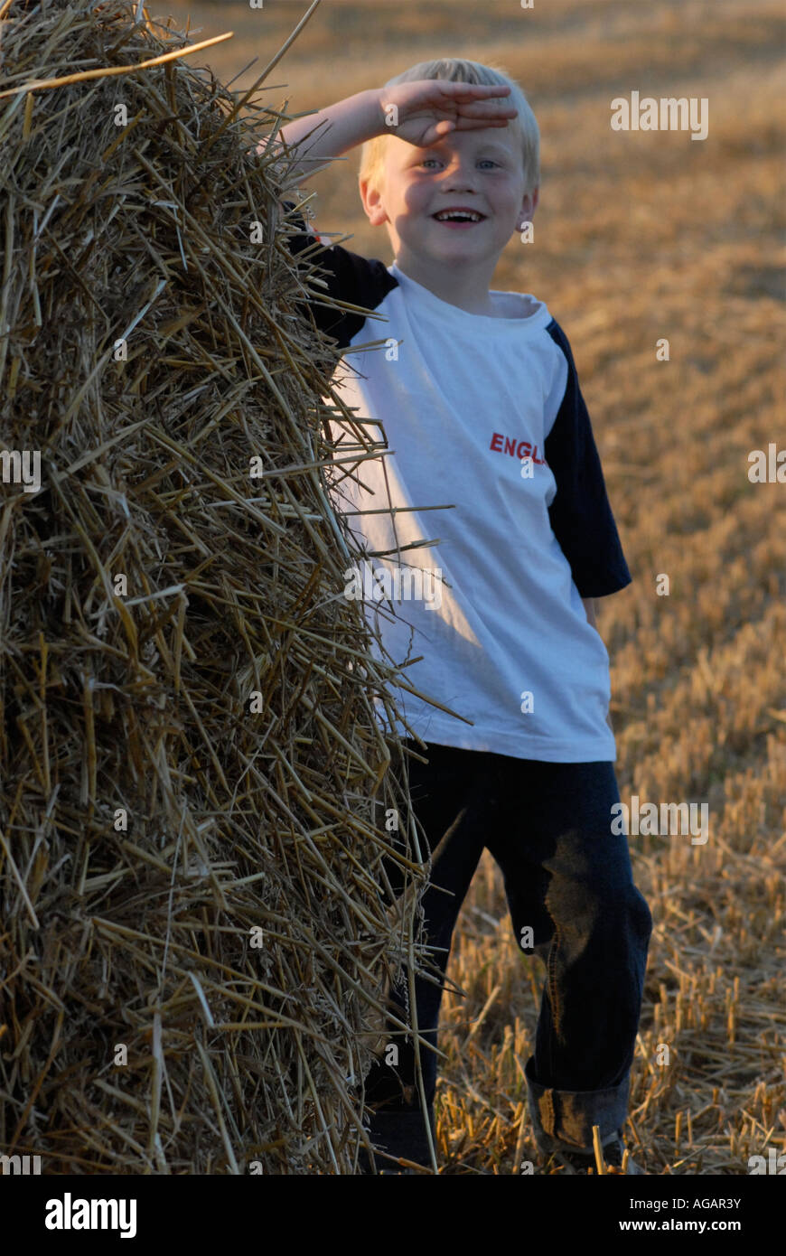 Portrait of a little boy standing next to a round bale of straw ...