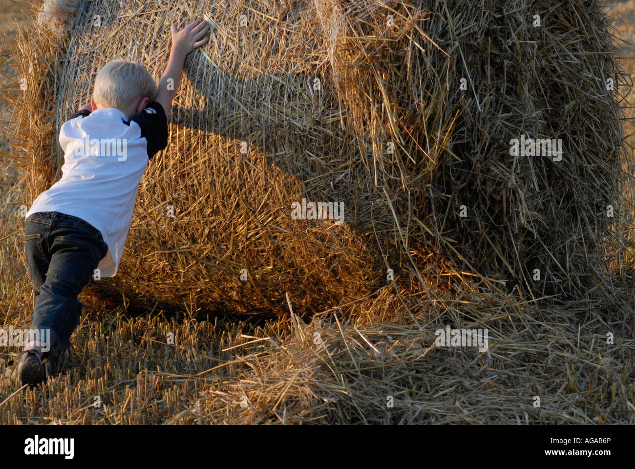 Little boy pushing a round bale of straw Stock Photo - Alamy