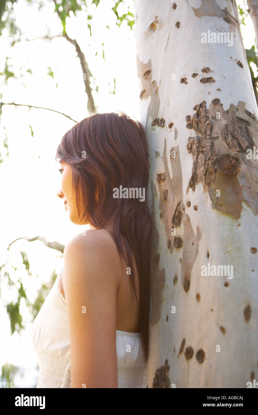 Young woman standing and leaning to tree Stock Photo - Alamy