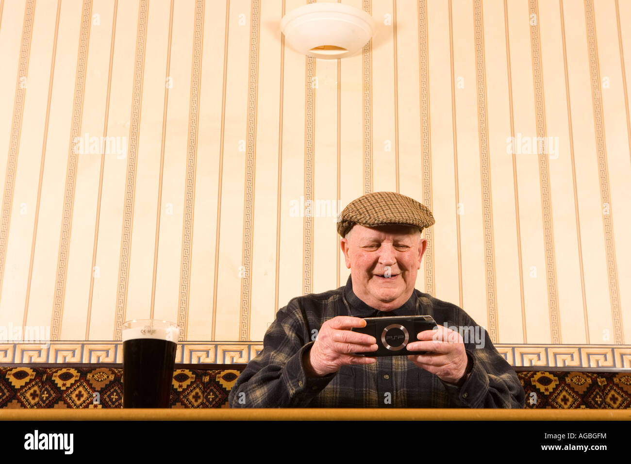 Old man wearing flat cap in pub playing with sony psp playstation with ...