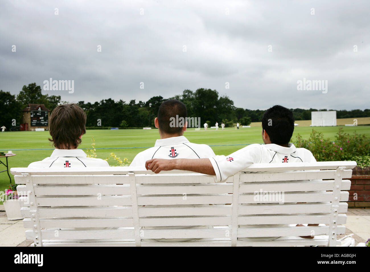Three males looking on at cricket match while sat on bench Stock Photo ...