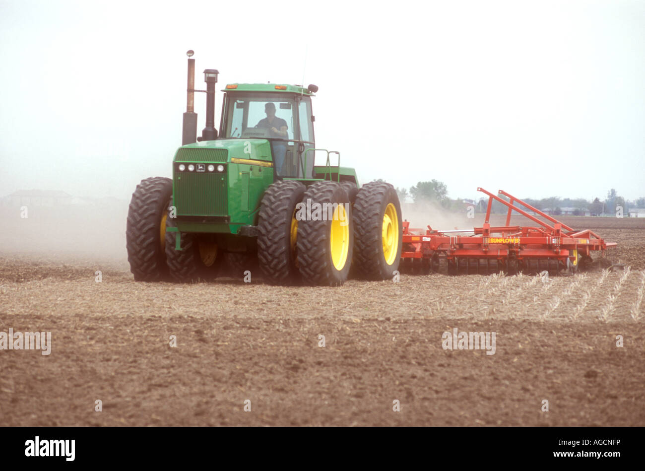 John Deere tractor tilling a farm field in spring to prepare for ...