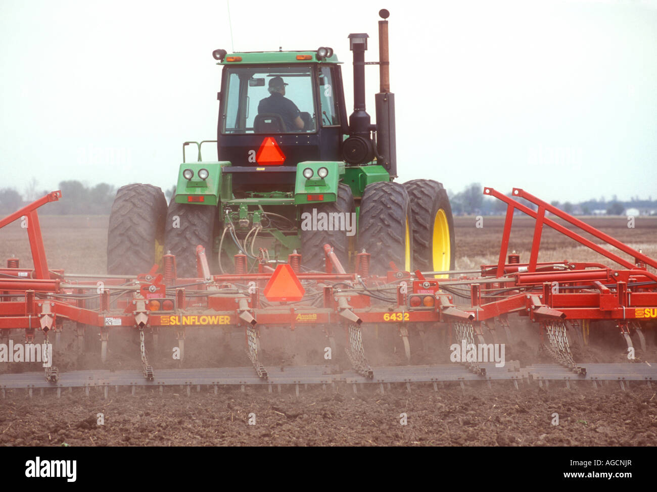 John Deere tractor tilling a farm field in spring to prepare for ...