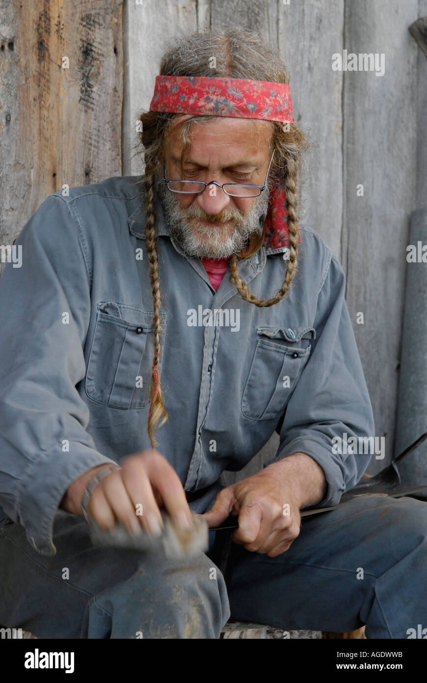 Stock image of a man with long braided hair peening and sharpening or ...