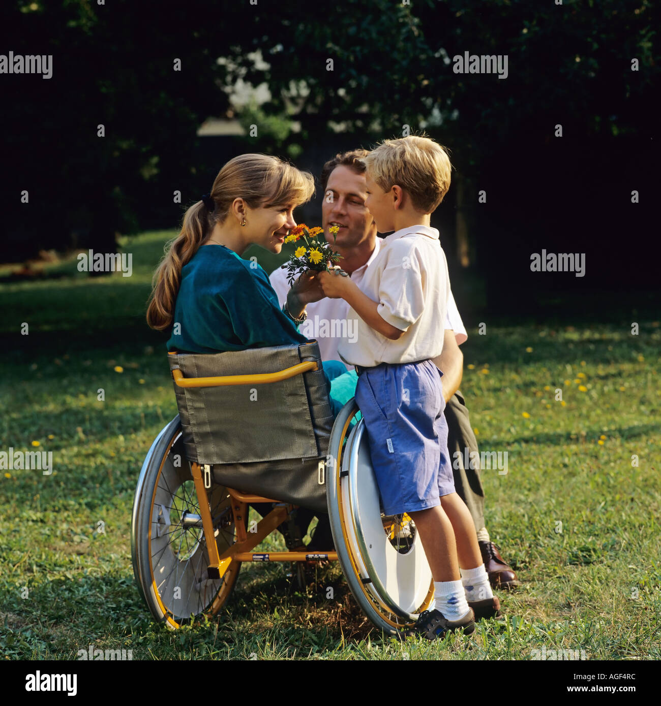 Little boy giving flowers to disabled woman in wheelchair and man in ...