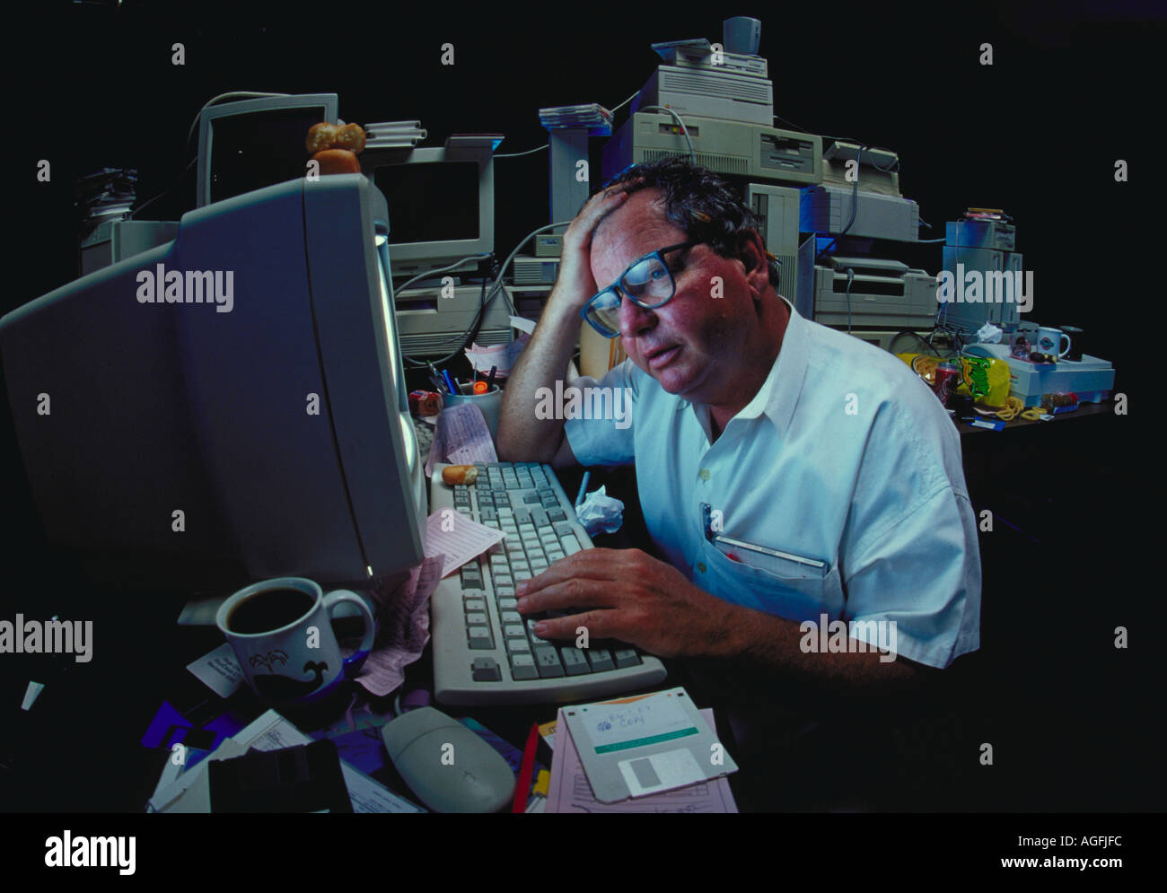 An overwhelmed worker sitting at a computer with more computers in the ...