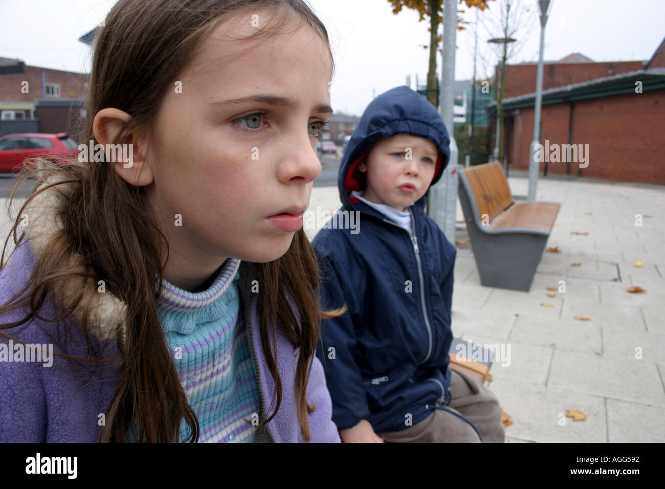 sulky looking girl aged 8 and questioning boy aged 4 sitting on a bench ...