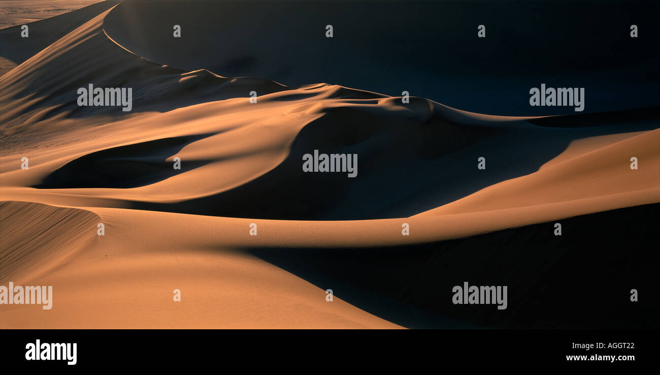 Namibia Namib Desert Setting sun lights curving sand dunes near coastal ...