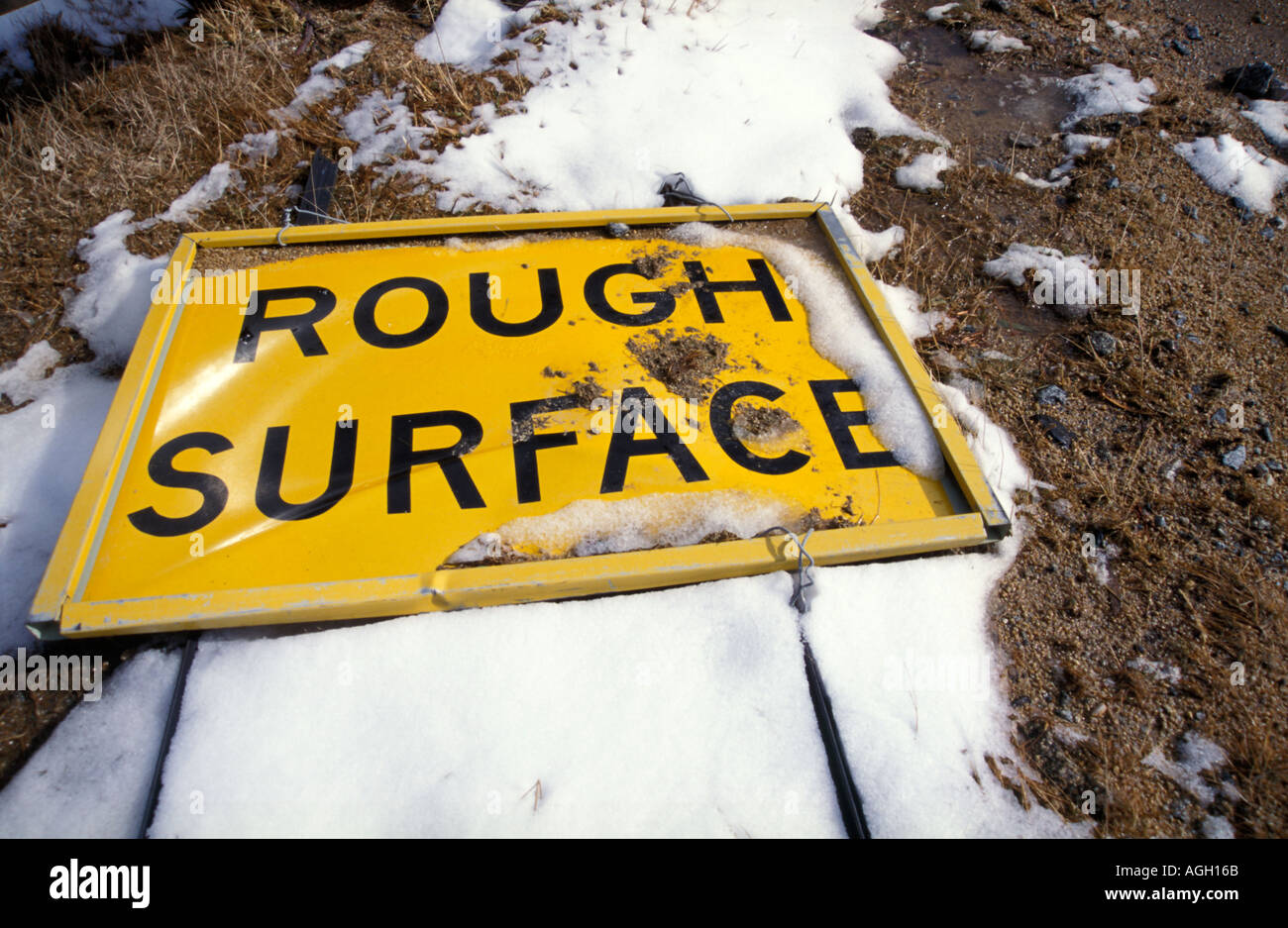 Rough surface warning road sign on a snow and grass background next to ...