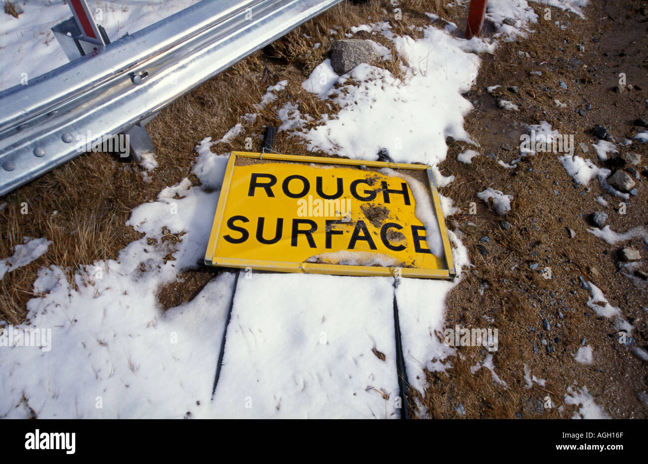 Rough surface warning road sign on a snow and grass background next to ...