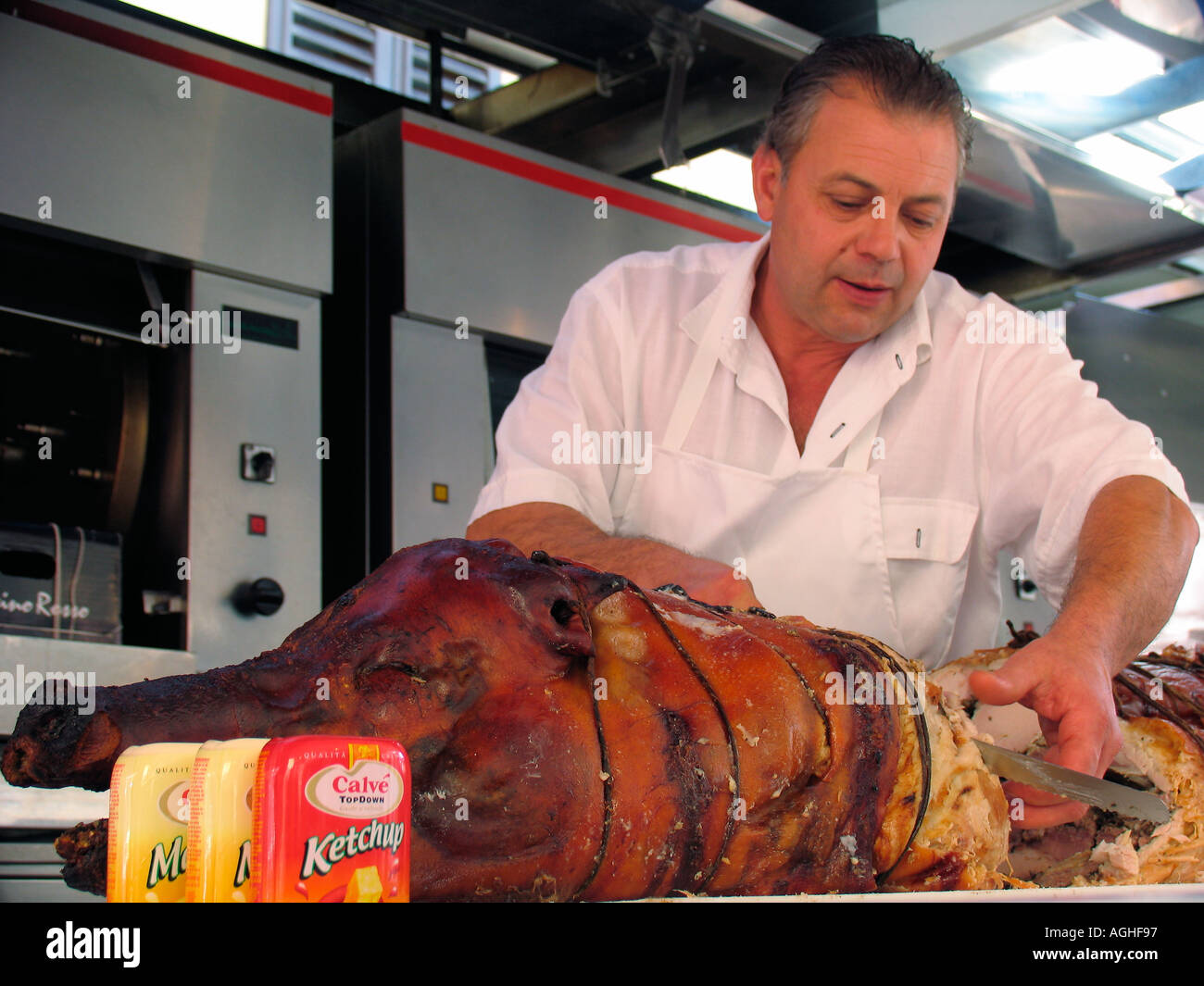 Butcher carving whole roast pig on counter in mobile meat market at ...