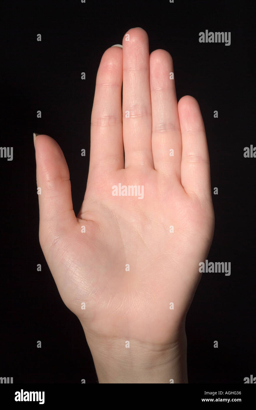 Left hand with thumb protruding raised against a black background to ...