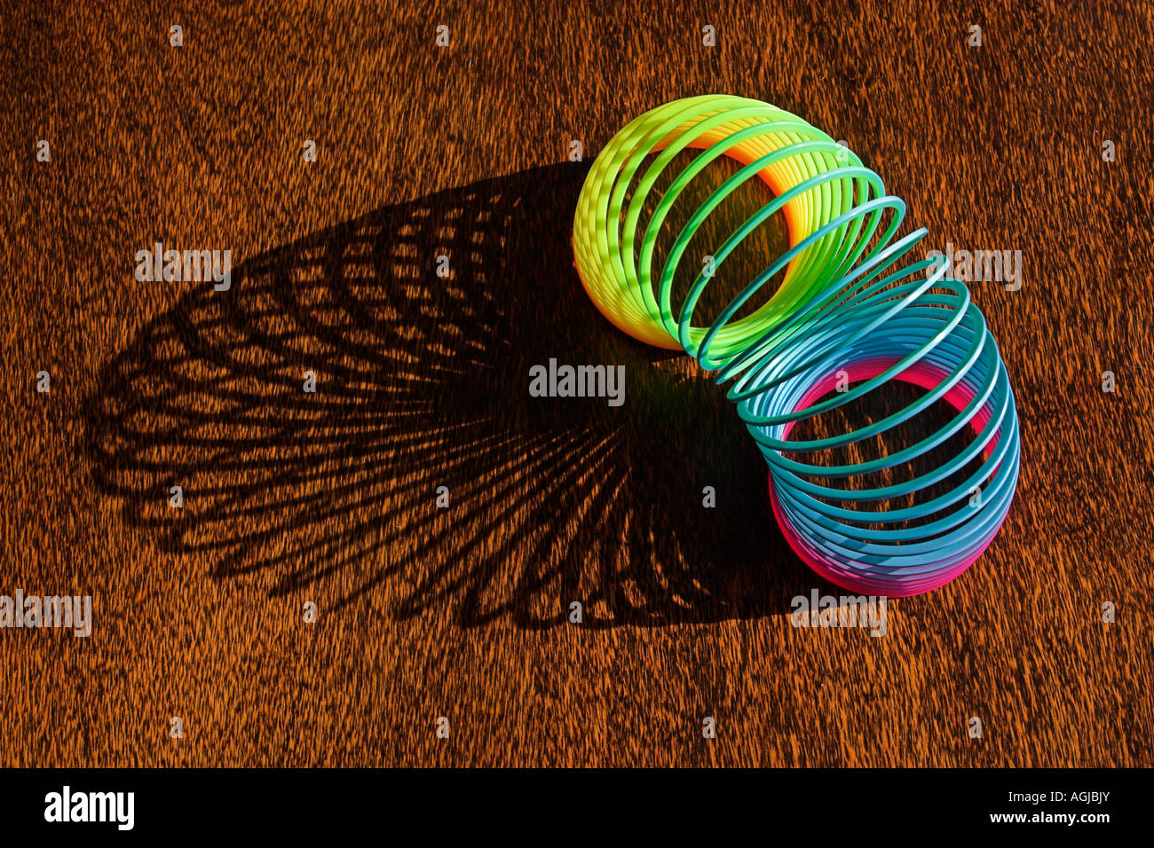 A childs toy slinky casts a shadow on a wooden table Stock Photo - Alamy
