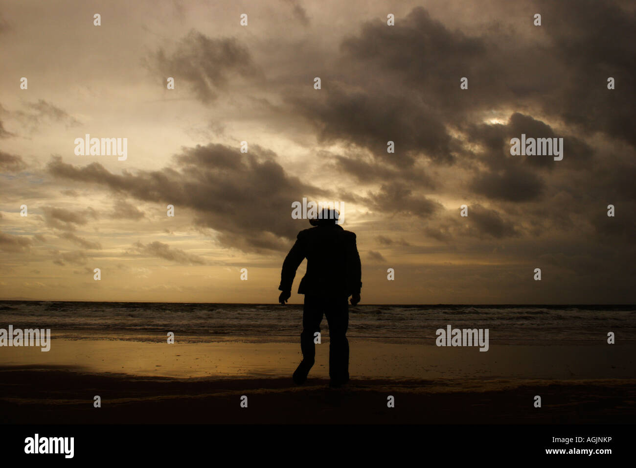 Man being buffeted by the wind on a stormy beach against a dramatic sky ...