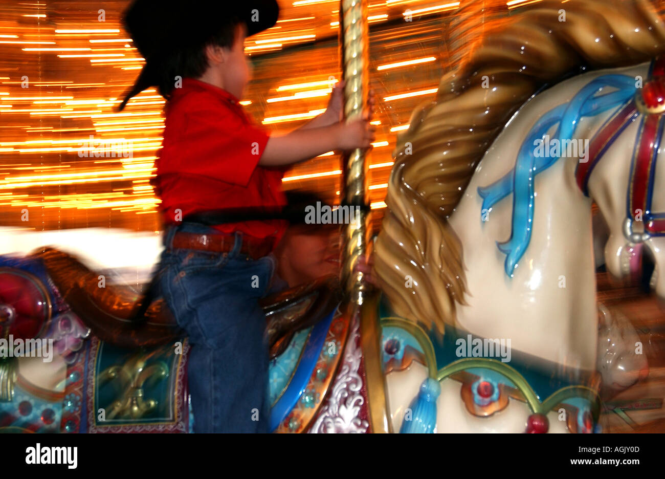 Boy wearing cowboy hat riding a carousel horse amusement park ride at ...