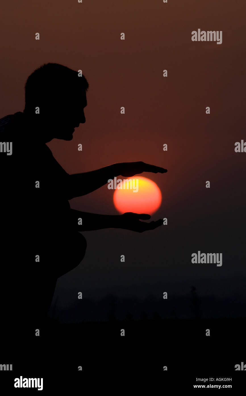 Young man silhouetted with hands around a sun that is setting Stock ...