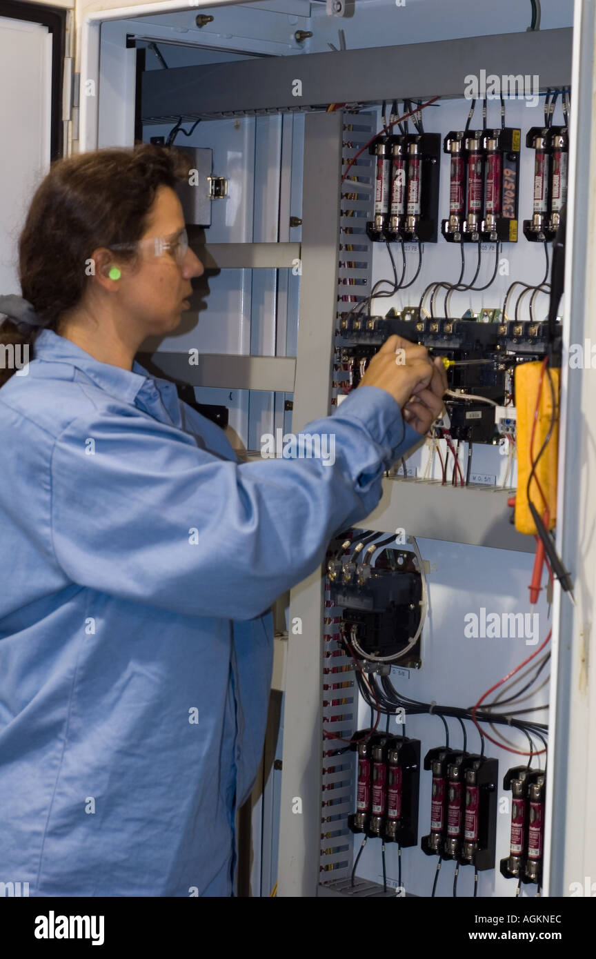 A woman electrician working on an electrical cabinet wearing ear plugs ...