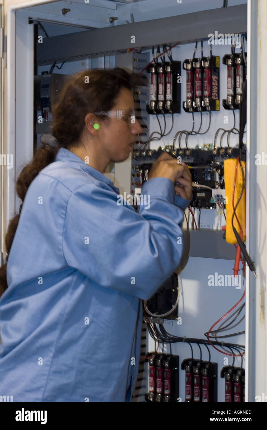 A woman electrician working on an electrical cabinet wearing ear plugs ...
