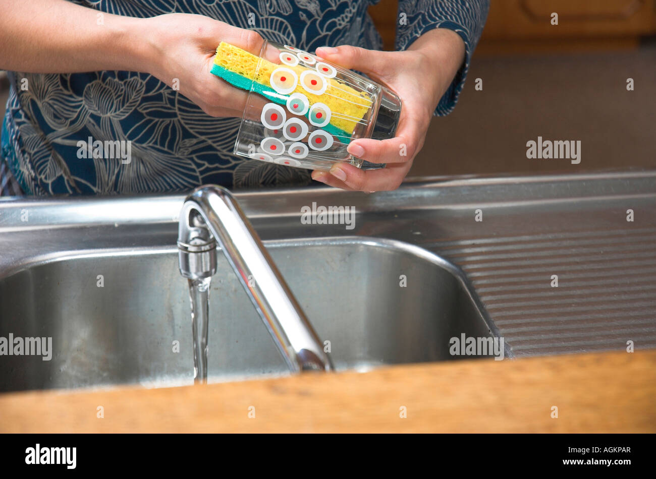 Woman washing a glass at the kitchen sink while water runs from the tap ...