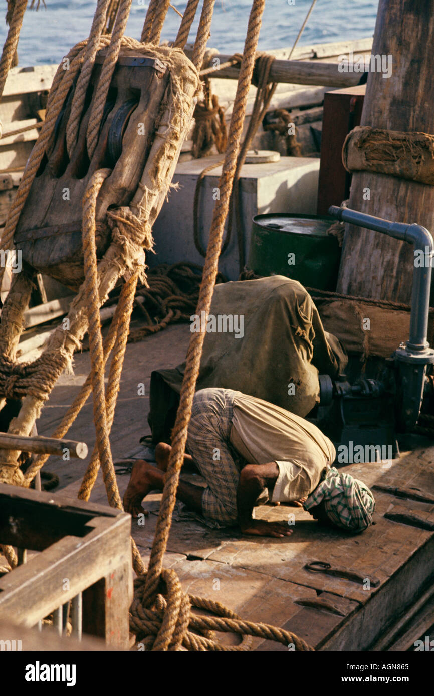 On the deck of an Arab dhow a sailor prays towards Mecca beside a huge ...