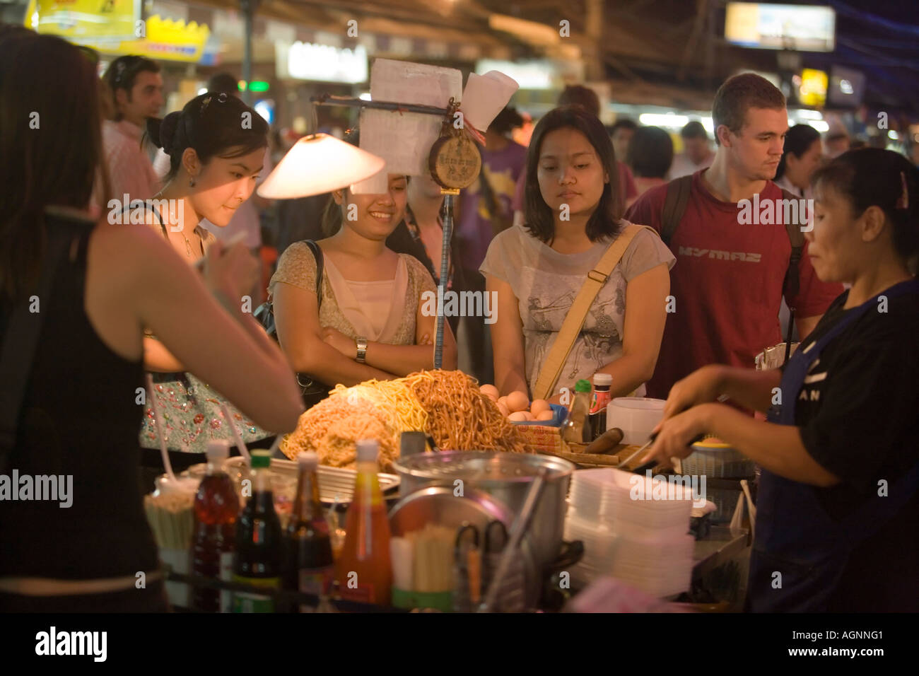 People standing around a food stand at Th Khao San Road in the evening ...