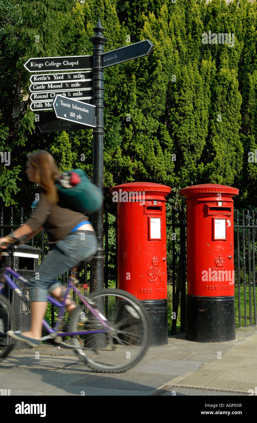 Cyclist riding on pavement past two red post boxes in Cambridge England ...