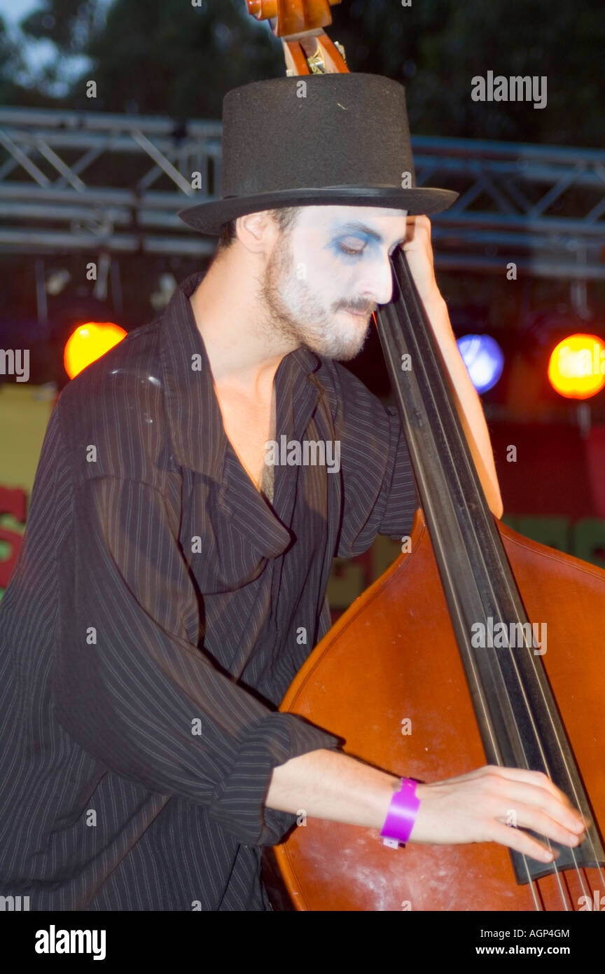 Musician dressed and made up as a clown playing a contrabass on stage ...
