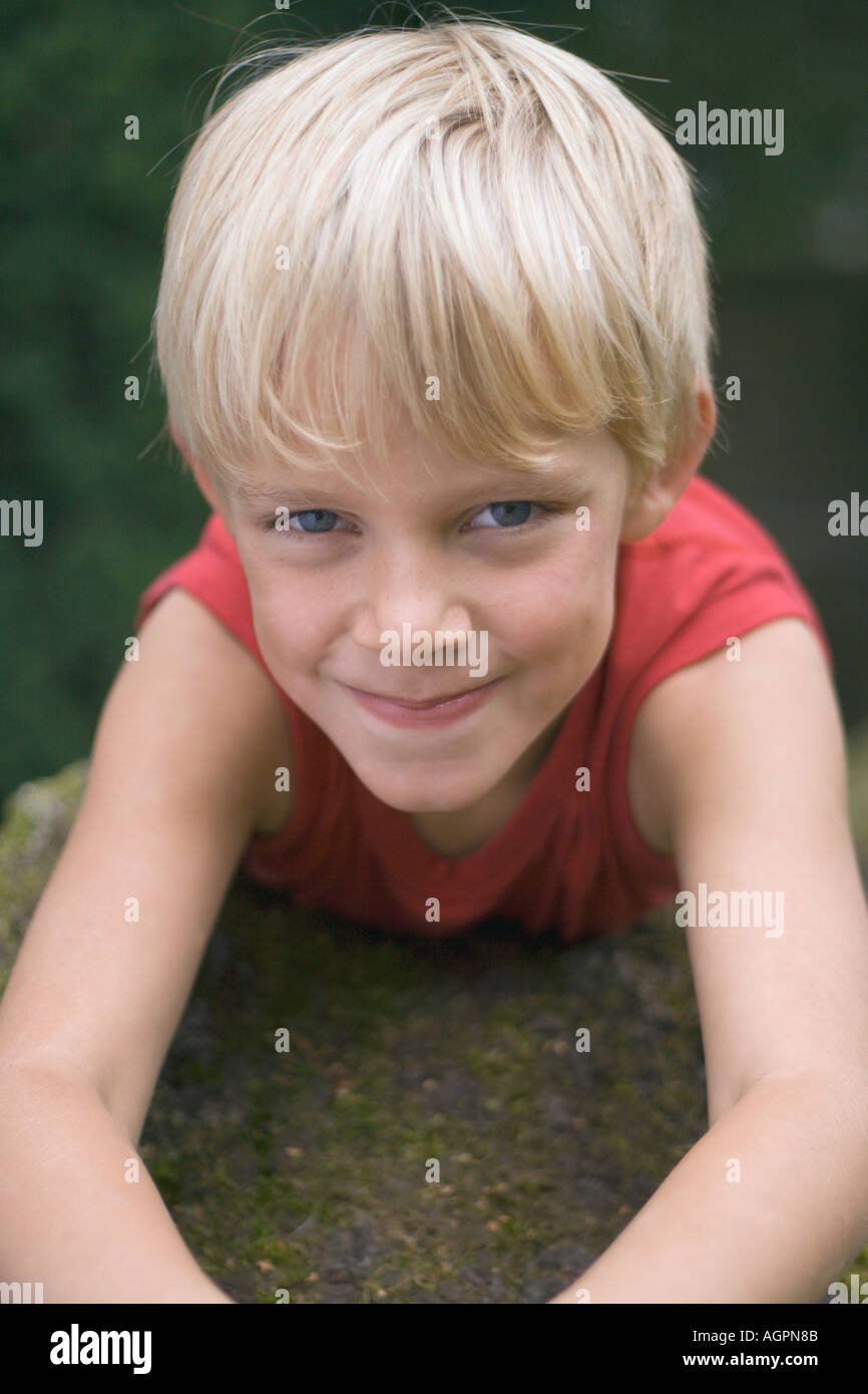 Boy with cheeky grin leaning forwards on a tree stump in Fjellerup ...