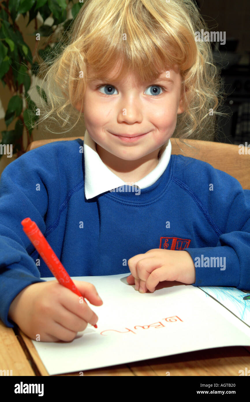 Little girl doing homework using a red pen to write in school book ...