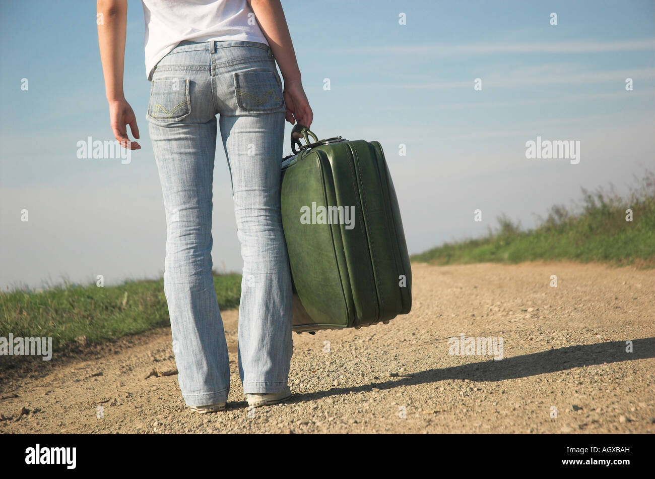 Young woman carrying suitcase on country road rear view Stock Photo - Alamy