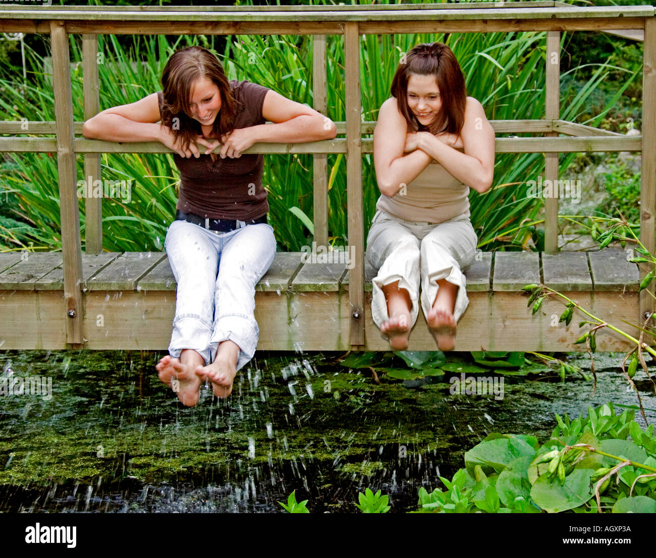 Two girls sitting on bridge over water. relaxing Stock Photo - Alamy