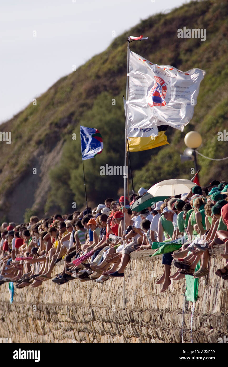 Spectators watching traineras regatta sitting on sea wall Puerto Viejo ...