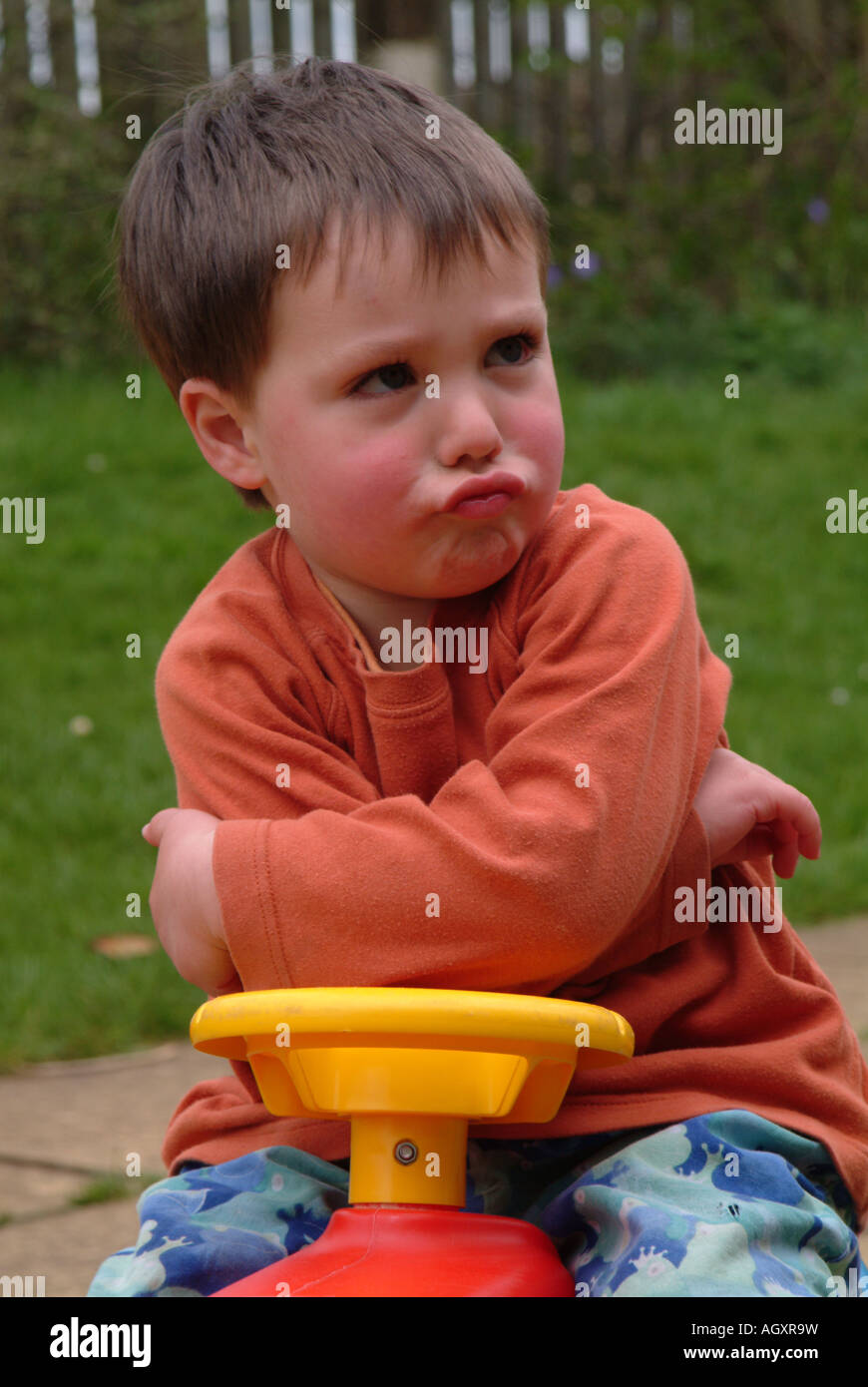 Toddler sitting on a ride on toy scowling Stock Photo - Alamy