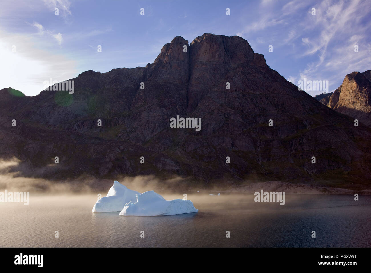 Dark mountain peak in shadow with small iceberg and wispy sea mist ...