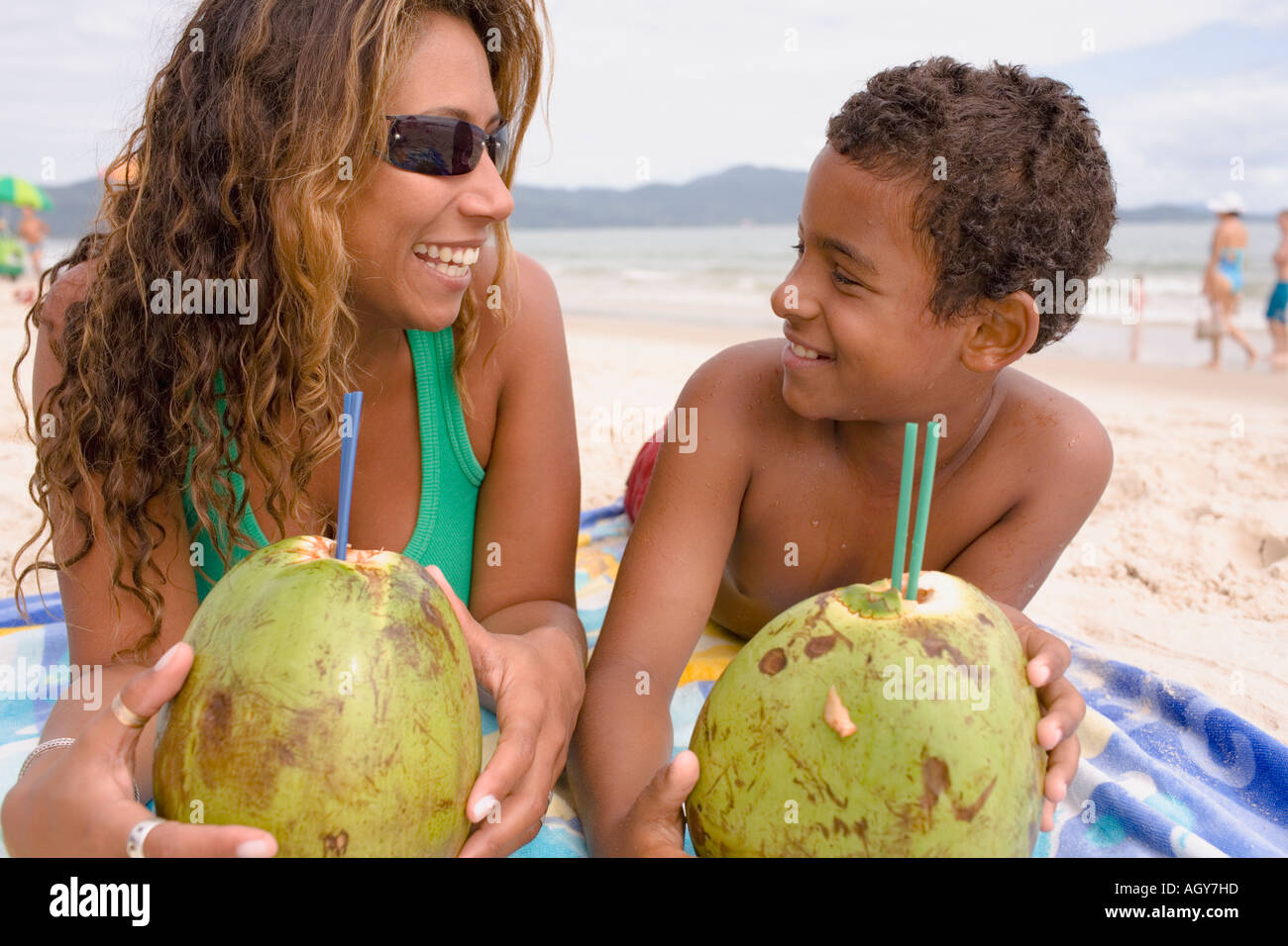 Hispanic mother and son lying on the beach drinking from coconuts ...