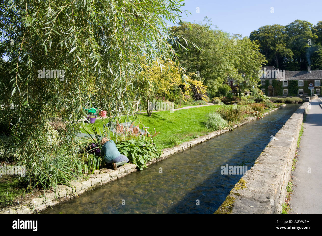 A gardener tending the grounds of Bibury Trout Farm beside the River ...