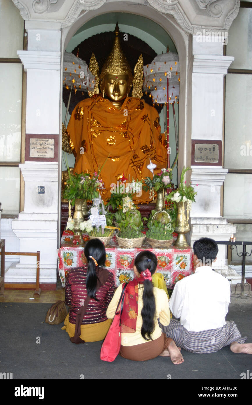 2 women and a man pray to an orange robed Buddha at Shwedagon Pagoda ...