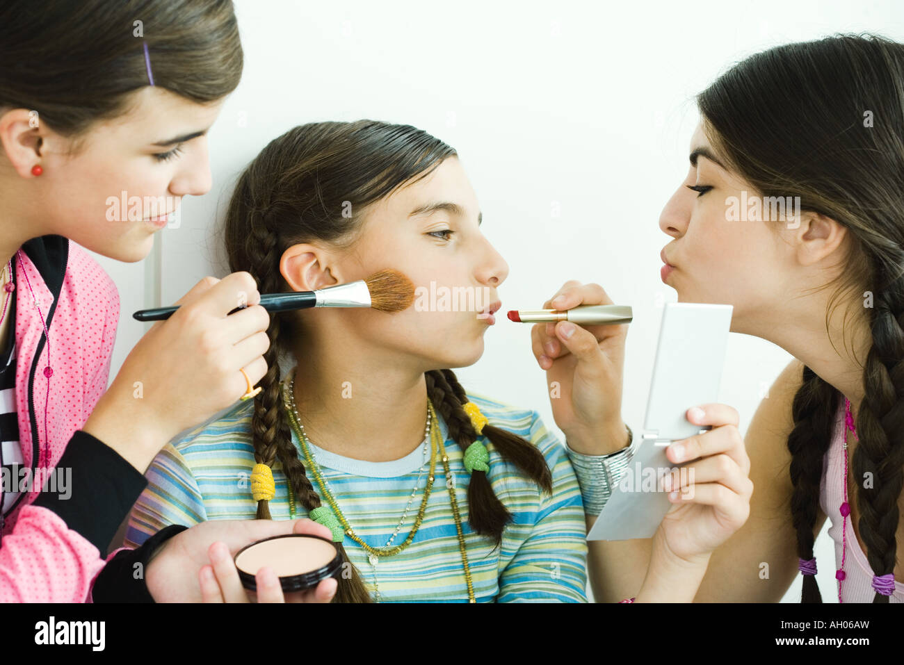 Two young female friends putting make-up on younger girl Stock Photo ...