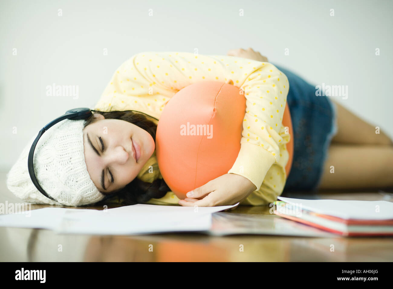 Young woman lying on floor listening to headphones, neglecting homework ...